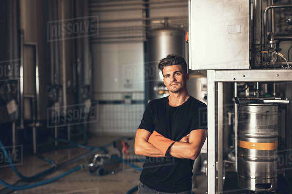 Portrait of young man standing by beer filling machine. Brewery worker ...