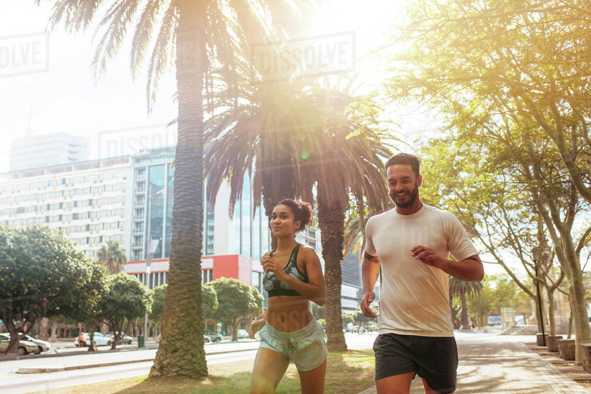 Young man and woman in jogging outfit running together outdoors. Couple ...