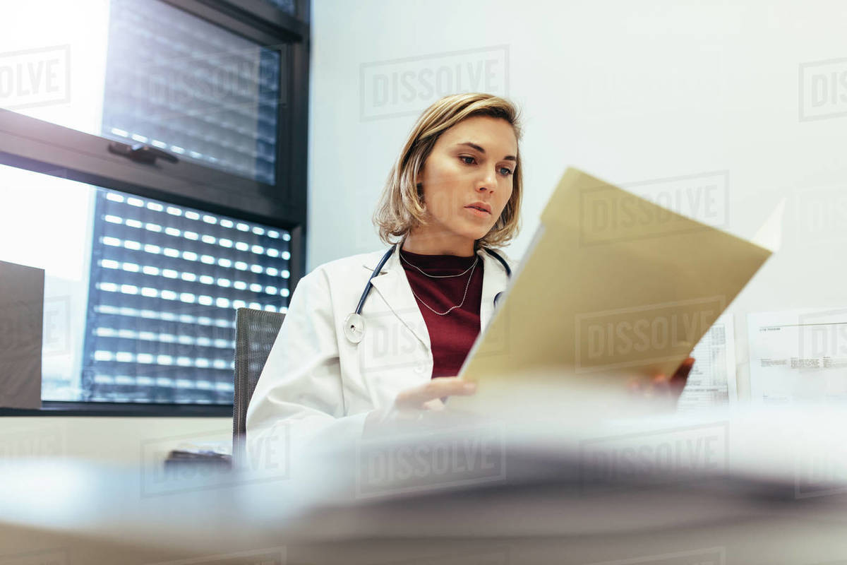 Female doctor sitting in her office and studying medical records ...