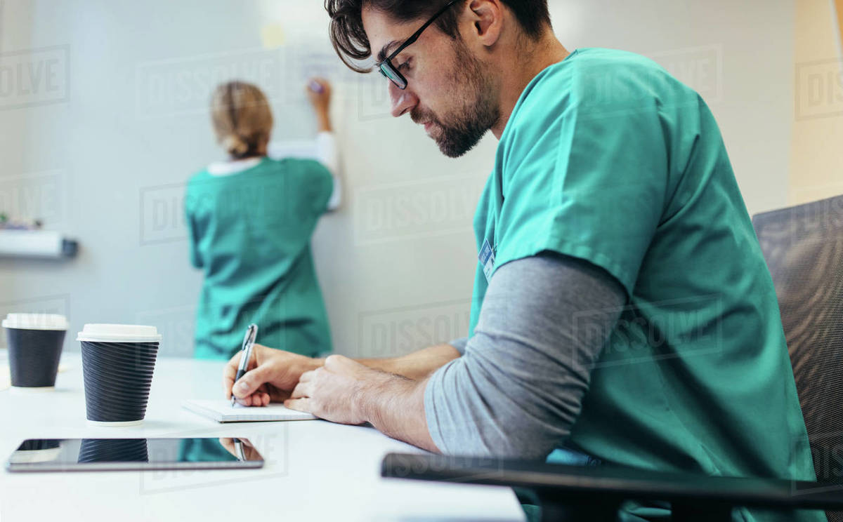Side view of healthcare worker sitting in hospital boardroom writing ...