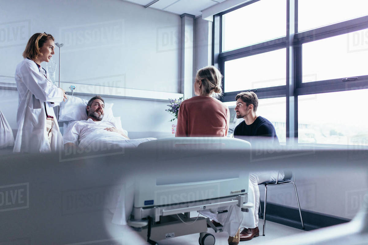 Female doctor visiting patient in hospital room. Male patient lying in ...