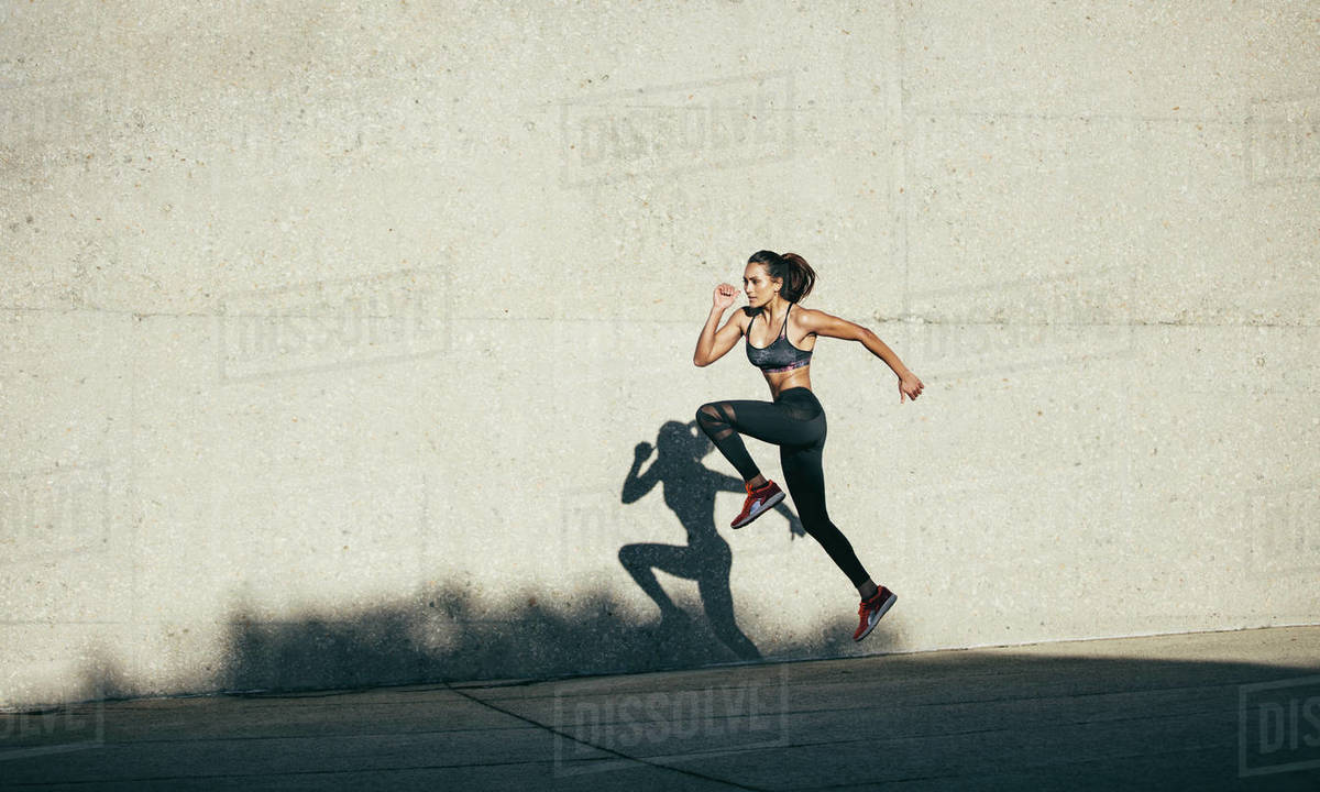 Healthy young woman running and jumping outdoors. Fitness model ...