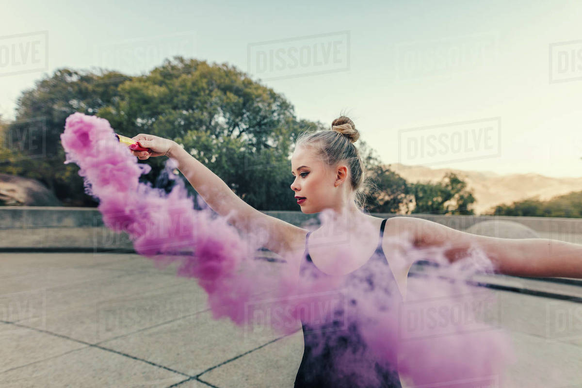 Ballet artist practicing dance moves outdoors using a pink smoke bomb ...
