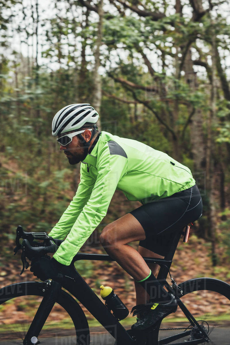 Side view of professional cyclist riding bike outdoors. Racer in green ...