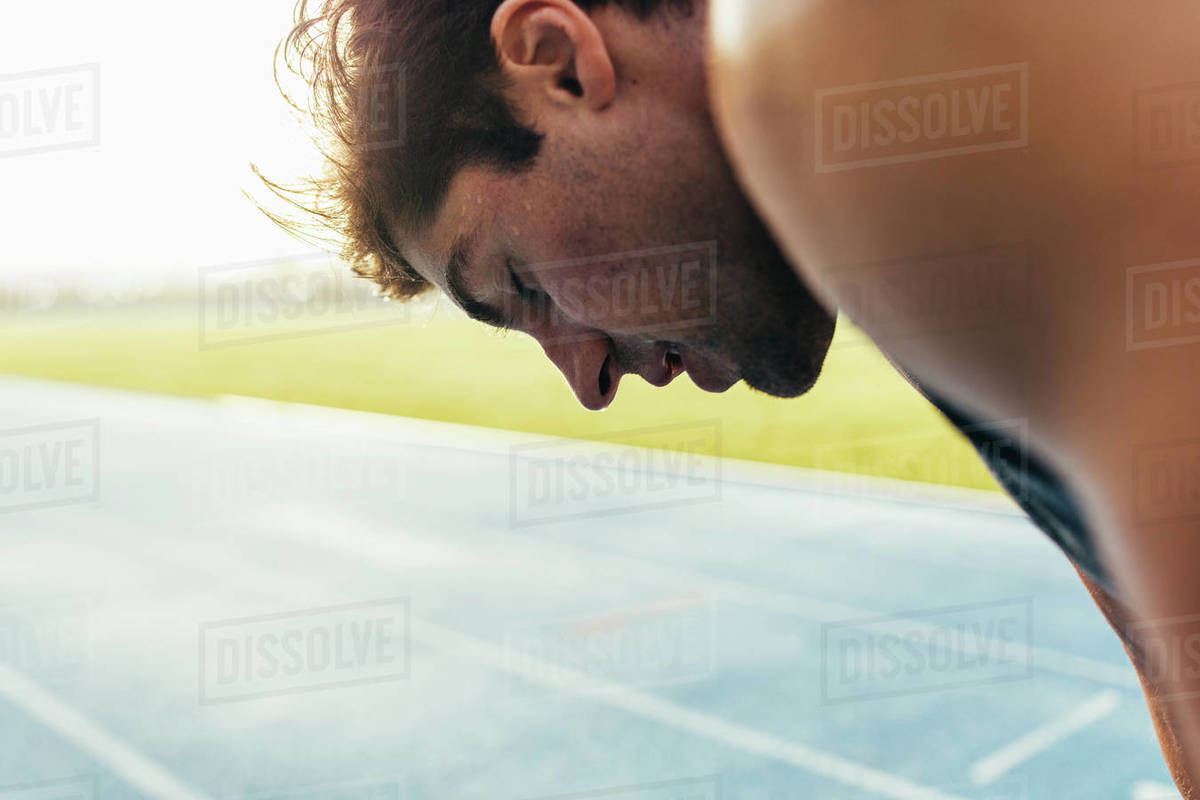 Closeup of a sprinter standing on a running track. Tired athlete ...