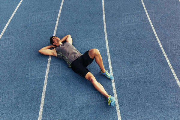 Runner lying on the track in a relaxed mood with hands under his head ...