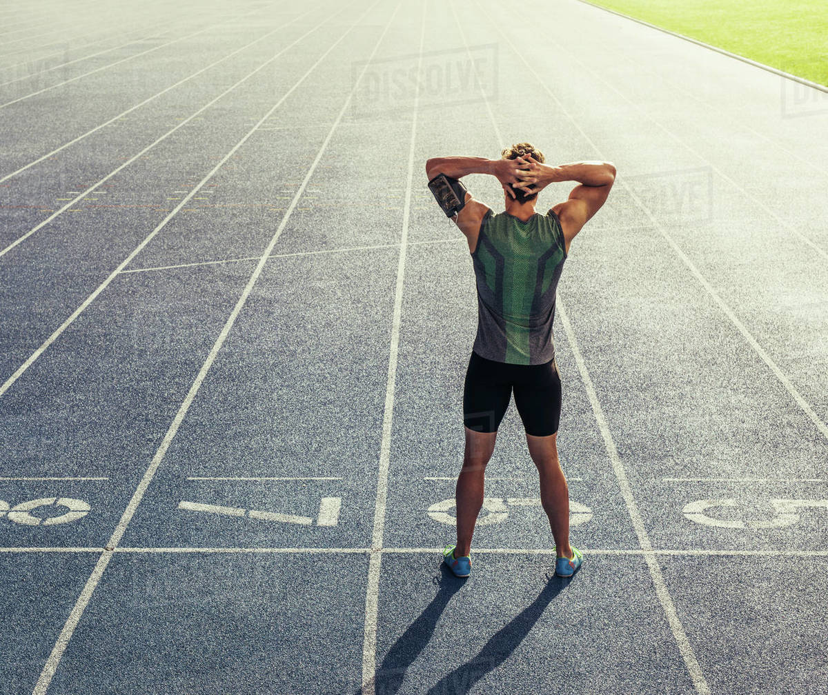 Rear view of an athlete standing on a running track with hands at the ...