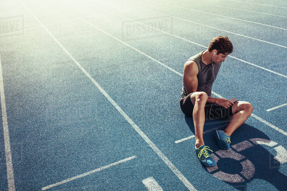 Athlete sitting on a running track listening to music. Runner wearing ...