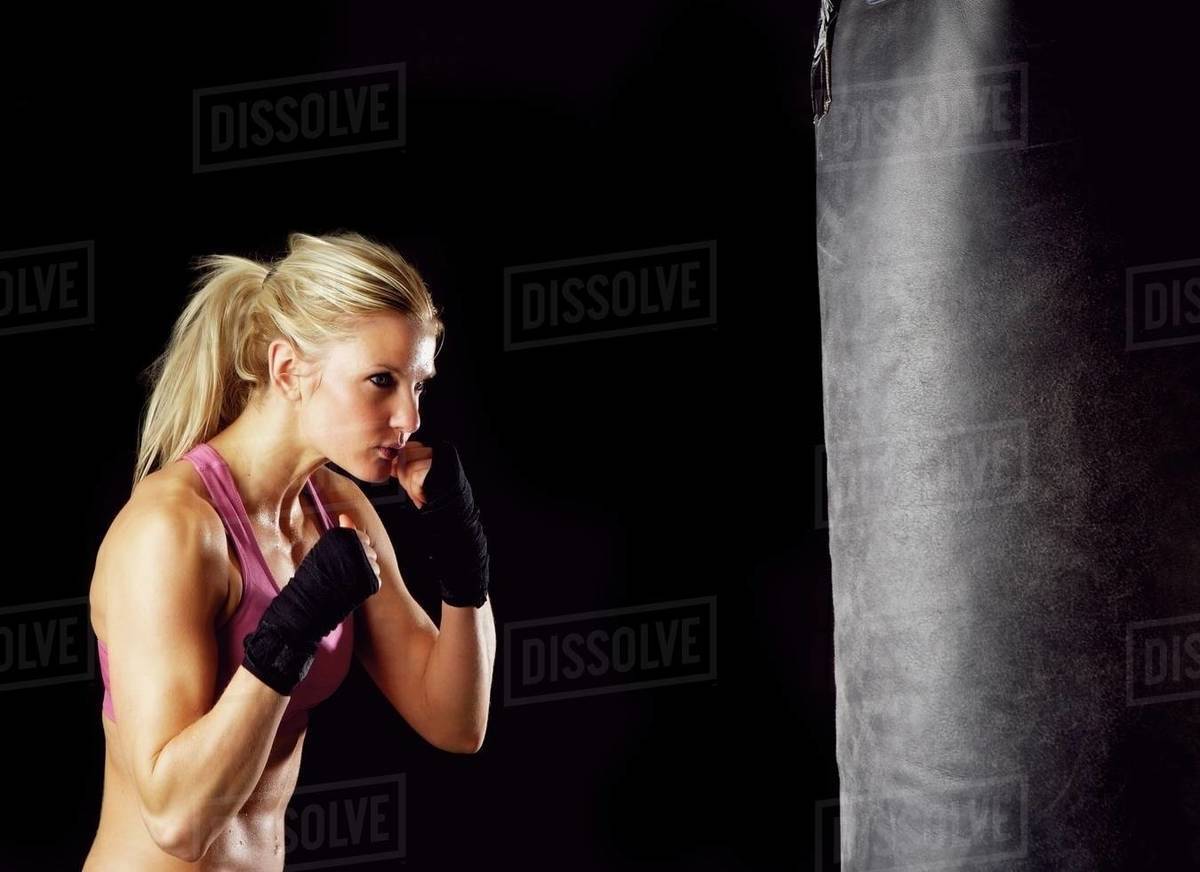 Young woman boxing on a punching bag. - Stock Photo - Dissolve