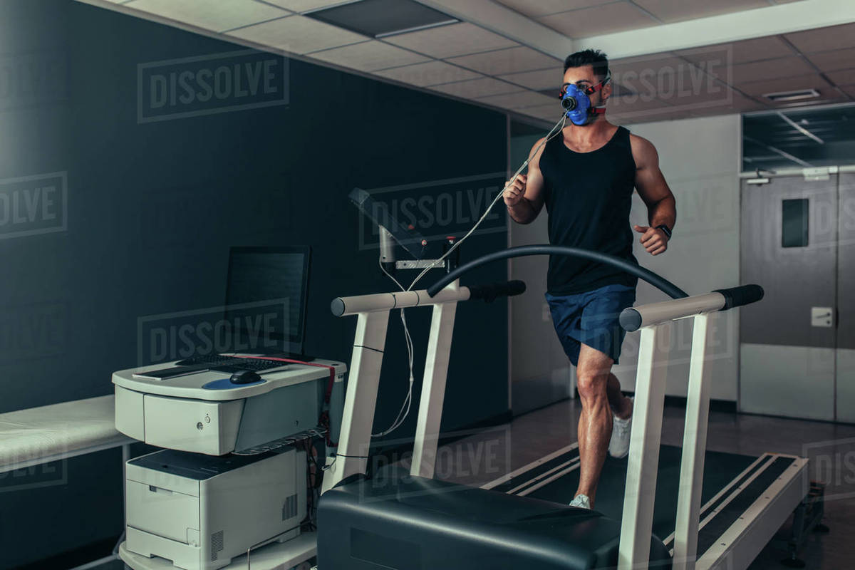 Male runner with mask running on treadmill machine testing his ...