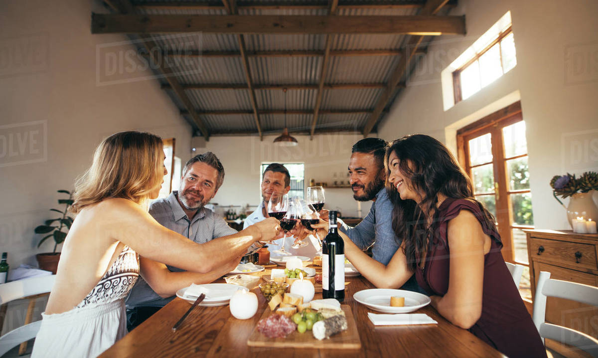 Friends sitting around a table having fun with wine and food. Group of ...