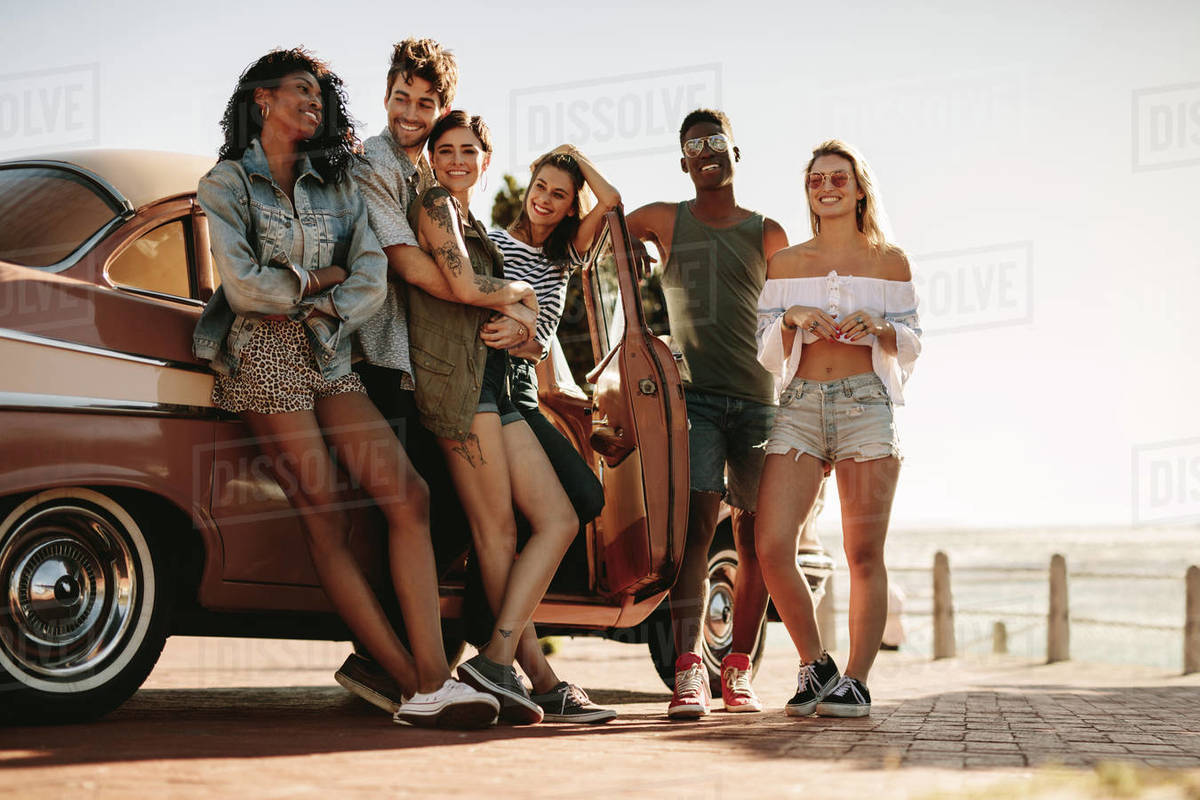 Group of young people on road trip standing by the car. Diverse group ...