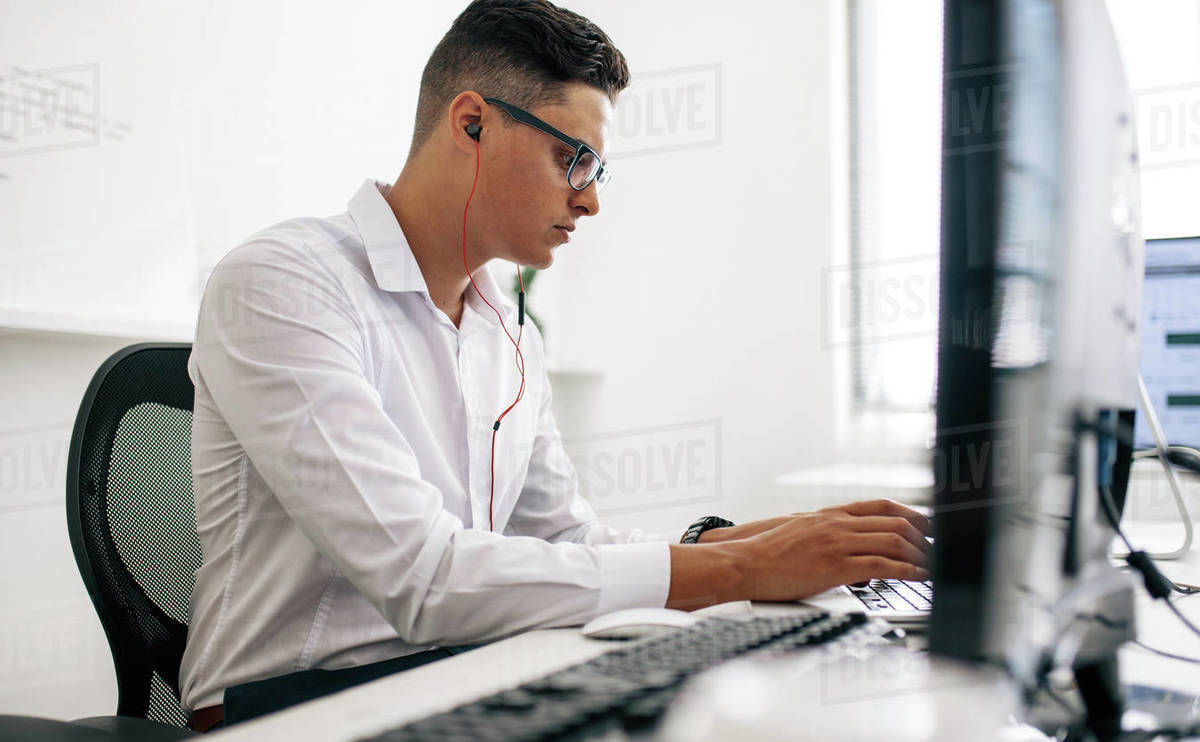 Software developer sitting at his office desk working on laptop wearing ...