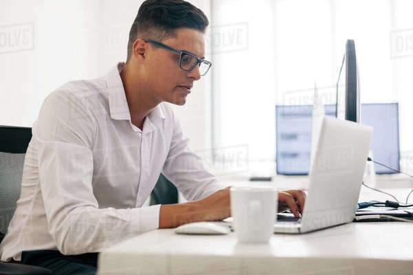 Software developer sitting at his office desk working on laptop ...