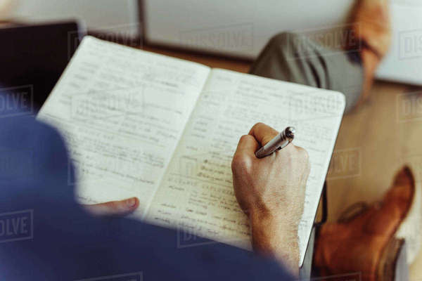 Rear view close up of man sitting on floor at home and making notes in ...