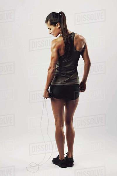 Fit and muscular woman with jumping rope standing on grey background ...