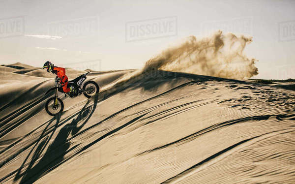 Motocross rider riding his racing bike down the sand dune. Motorbike ...