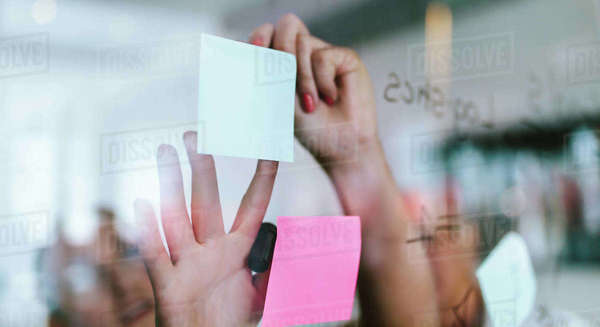 Hands of woman pasting sticky notes on glass wall in office. Business ...