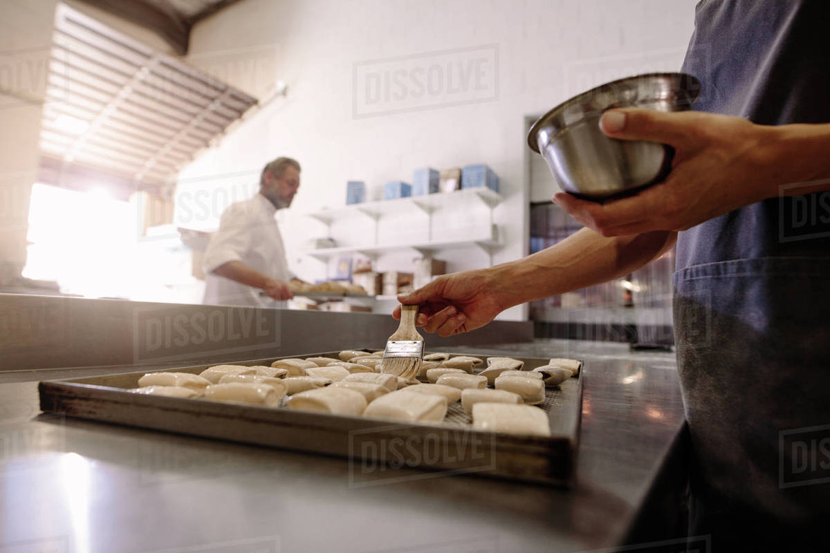 Hands of female baker smears butter with brush on rolls placed on ...