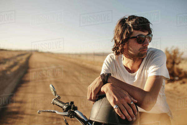 Portrait of young motor cycle rider leaning on his helmet and looking ...