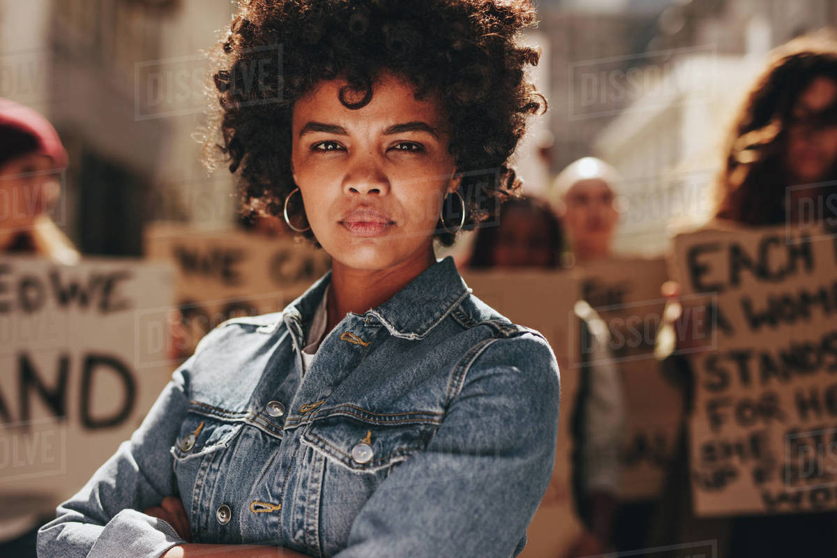 Young black woman with group of demonstrator in background outdoors ...