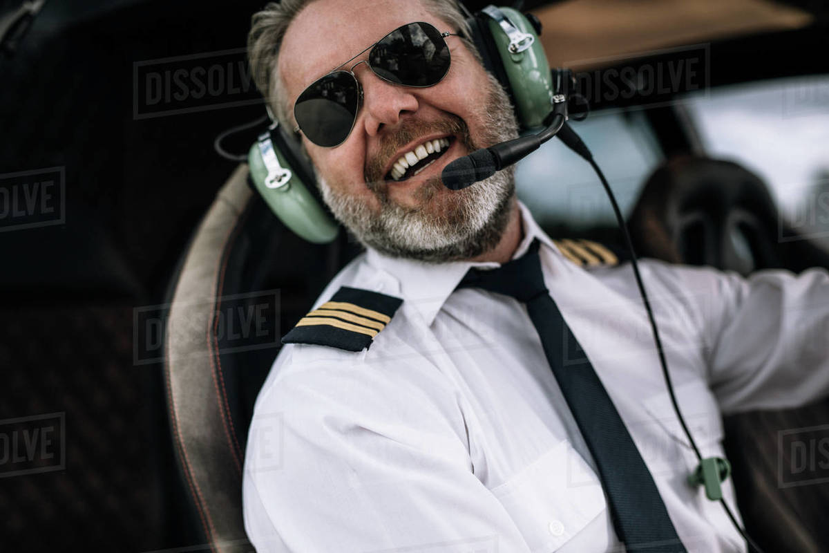Confident pilot with headset smiling in the private helicopter. Happy ...