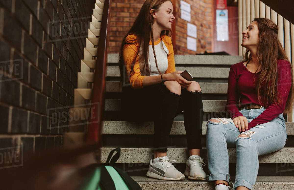Two young women sitting on college steps and talking. Best friends ...