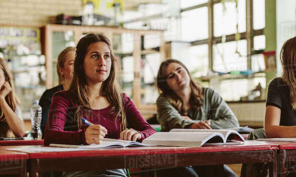 Beautiful young woman sitting in class with classmates around paying ...