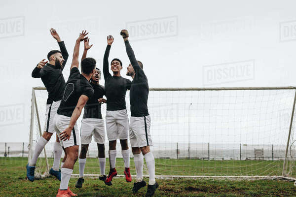 Excited football players jumping in excitement standing in a huddle ...