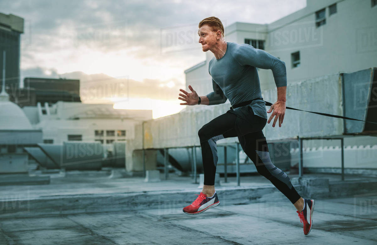 Fitness man running on terrace of a building with a resistance band to ...