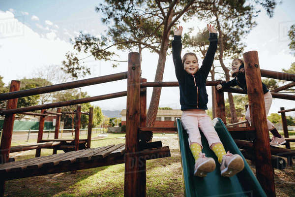 Two active girls playing together outdoors on the slide at the garden ...