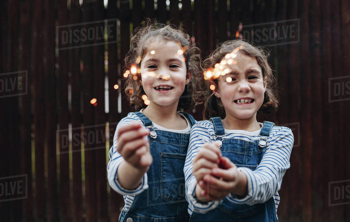 Two little girls holding sparkling hand fireworks. Identical twin ...