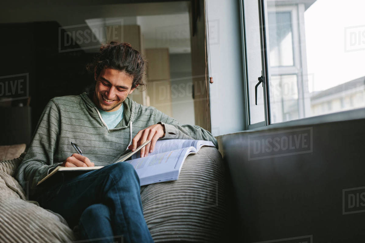 Smiling man sitting comfortably at home writing in a book. Student ...