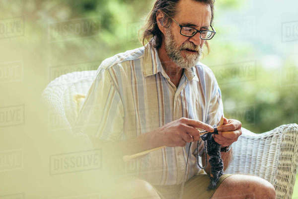 Elderly man with beard sitting on chair and knitting. Old man knitting ...