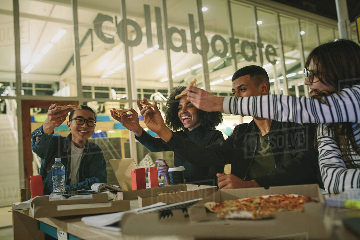 Multi-ethnic group of students eating pizza at university canteen ...