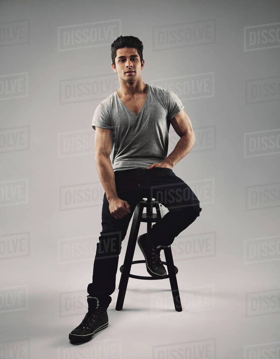 Full length portrait of handsome young man sitting on bar stool. Young ...