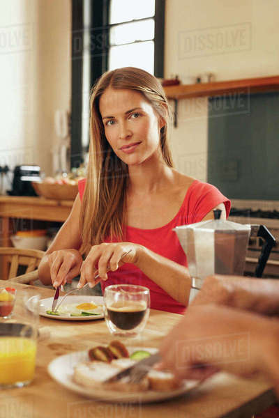 Portrait of attractive young woman sitting at breakfast table eating ...