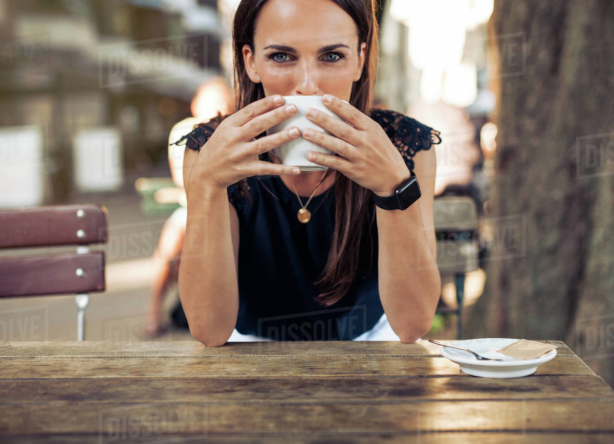 Young woman drinking coffee at a cafe and looking at the camera ...