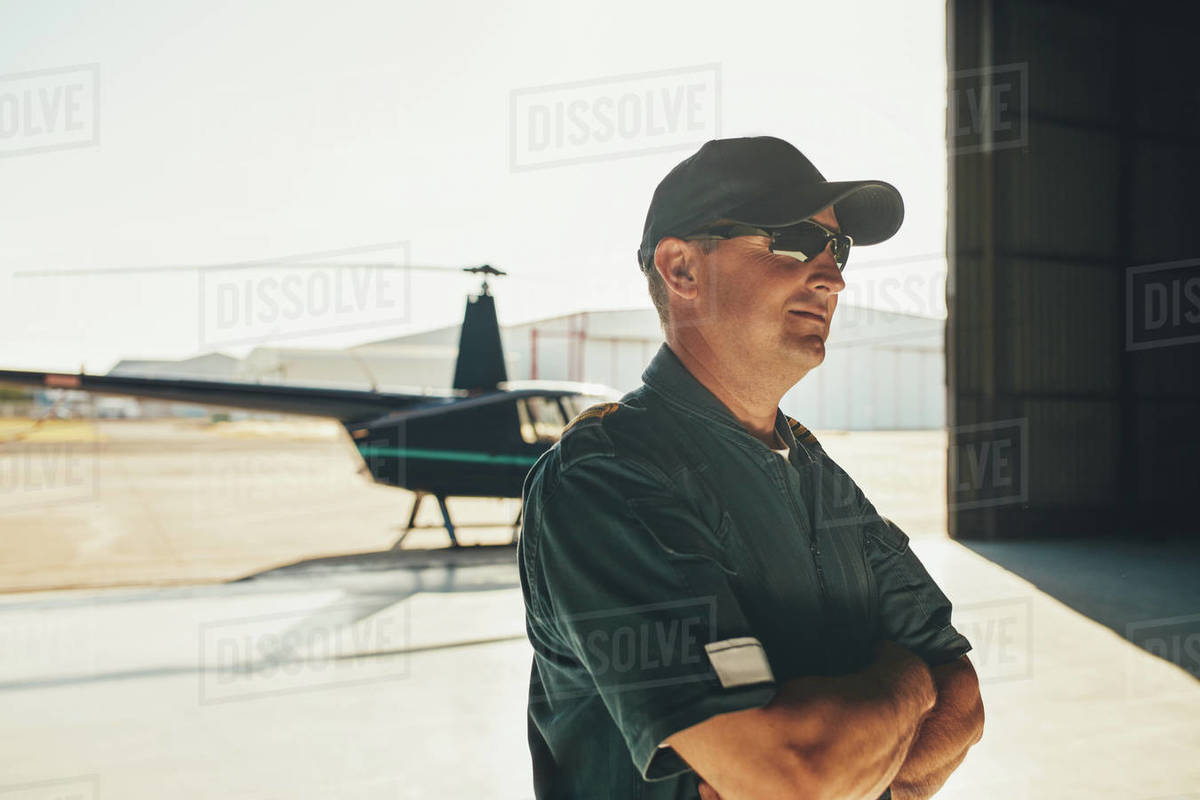 Portrait of helicopter pilot in uniform standing with his arms crossed ...