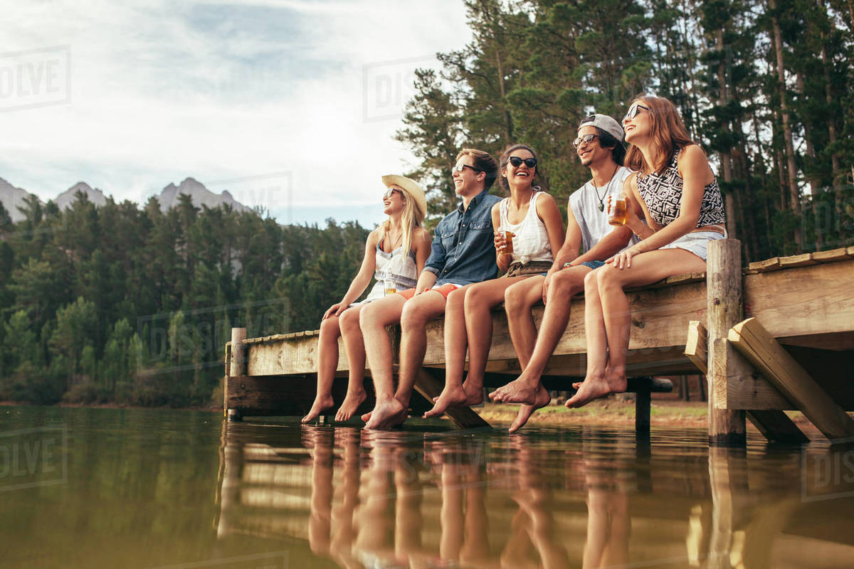 Group of happy young friends having fun and drinking beer while sitting ...