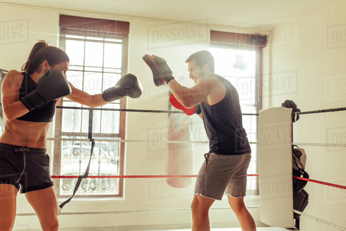 Muscular female boxer striking focus mits held by young male trainer in ...