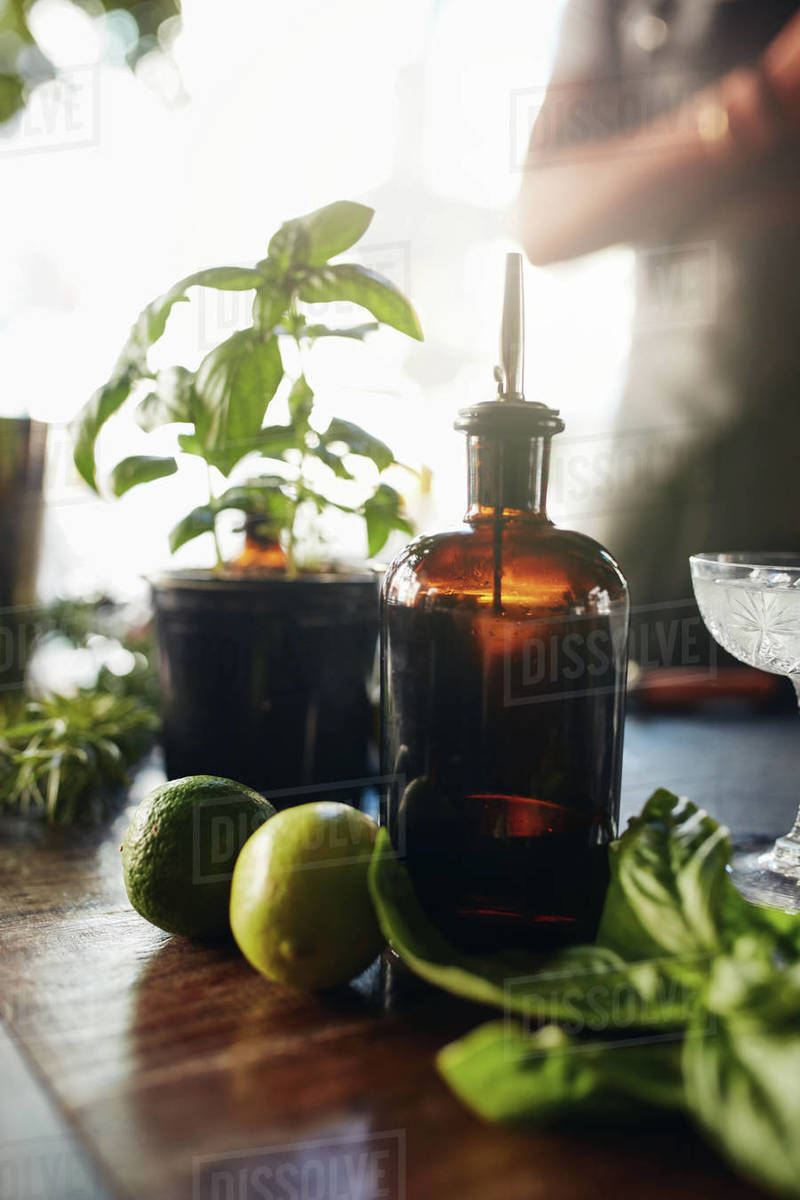 Close up shot of syrup bottle with lemons and basil leaves on bar table ...