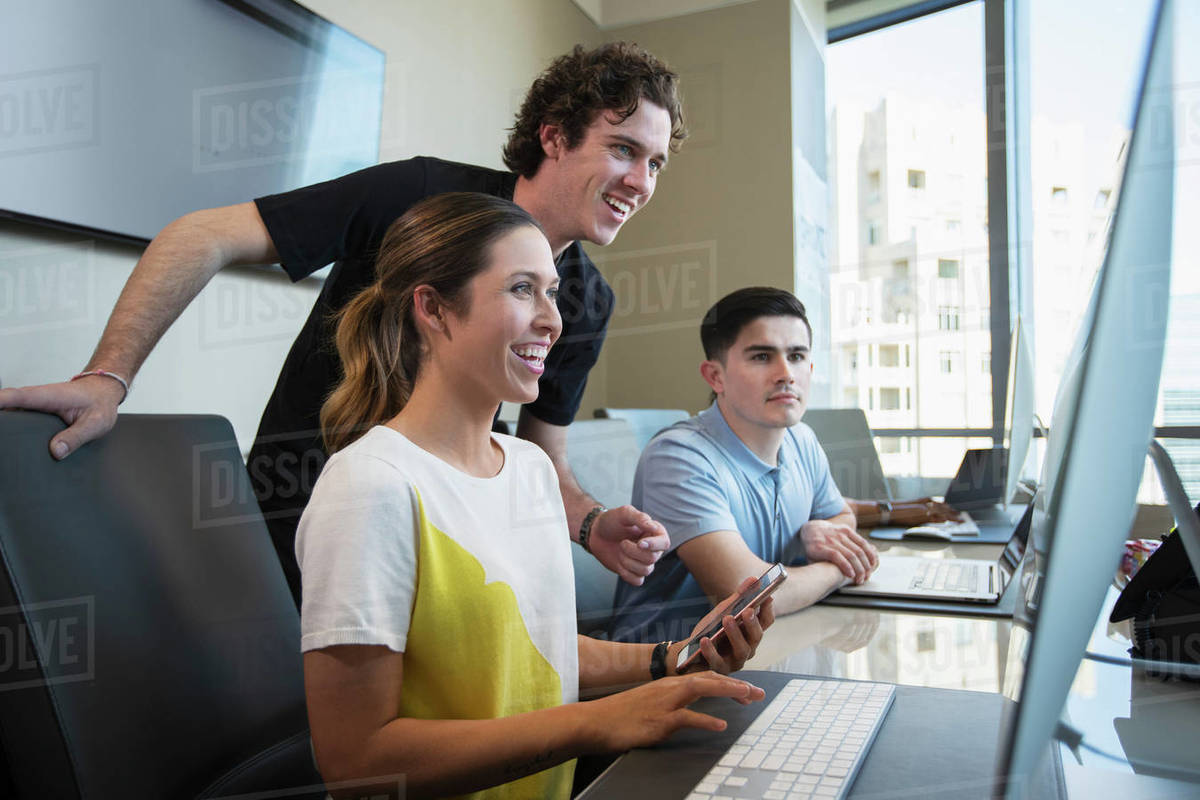 Young woman using computer in office holding mobile phone, showing male ...
