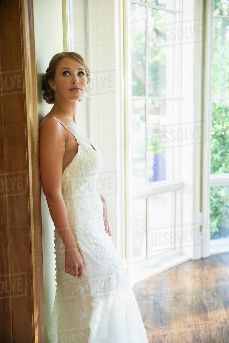 Portrait of young bride in home leaning on doorframe looking up towards ...
