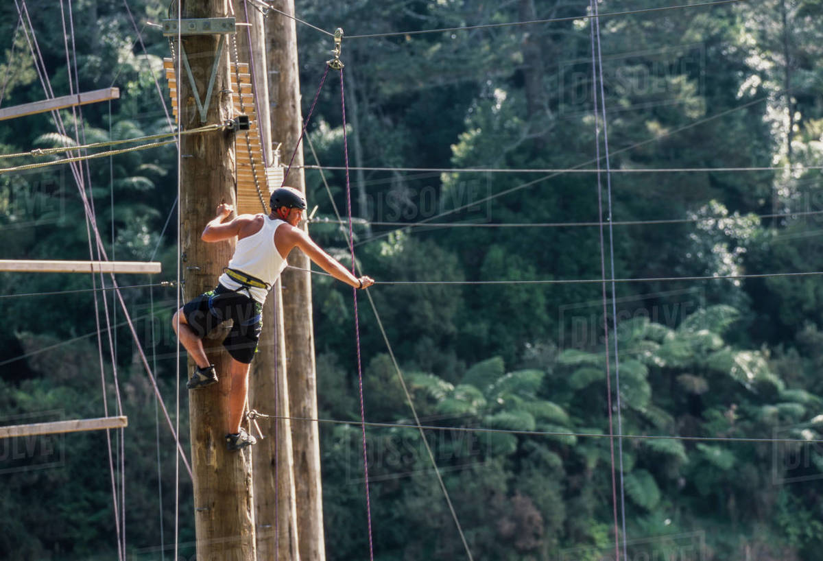 Man standing at top of poll ready to balance on suspended rope at ...