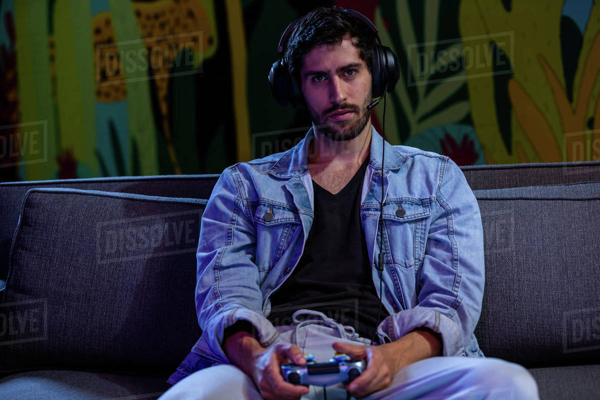 Man leaning back on couch with video game controller in hands, looking ...