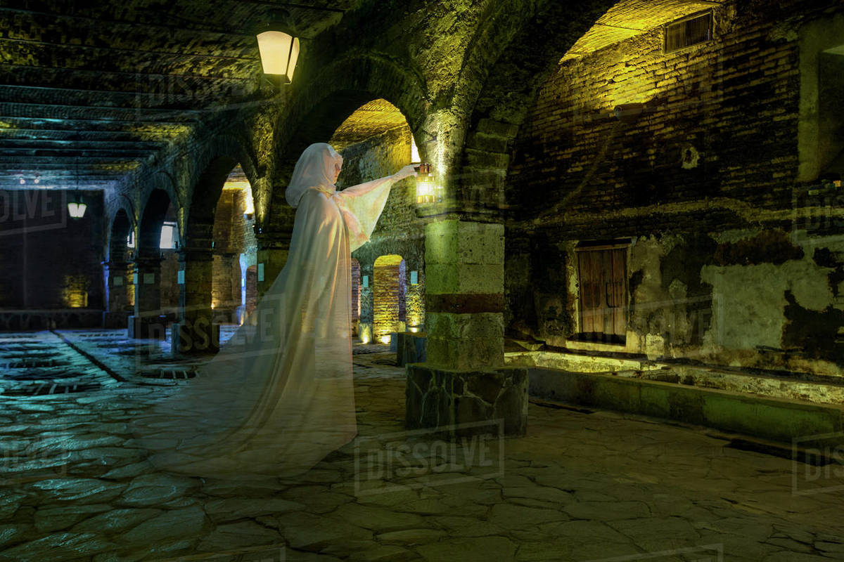 Female ghost with lantern, dressed all in white standing in a cavernous ...