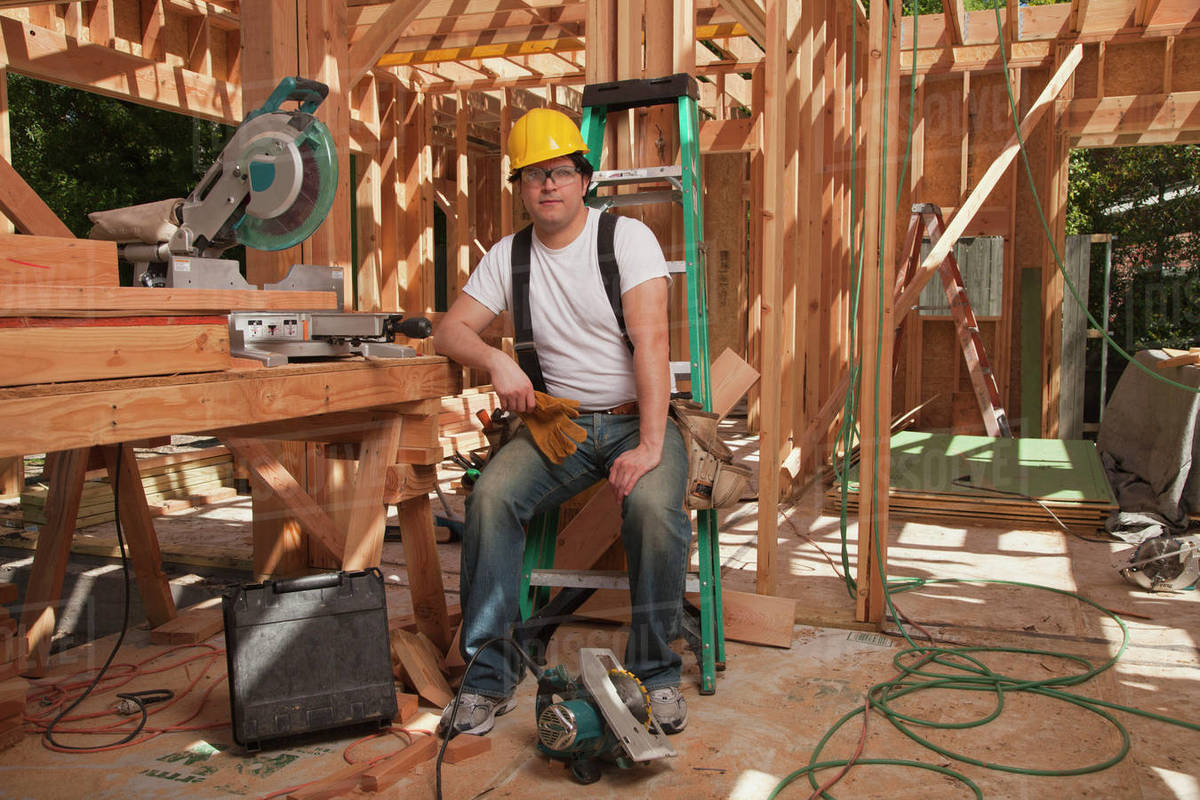 Man at a residential construction site sitting on a ladder and leaning ...