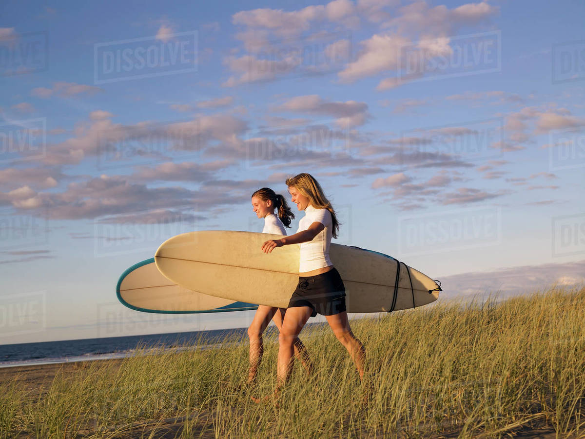 Two young women walking along the beach carrying surfboards - Royalty ...