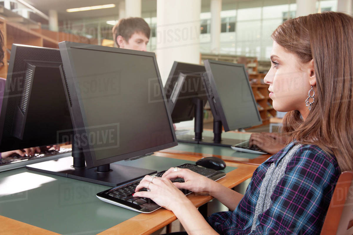 Female student typing at keyboard while at computer in library ...